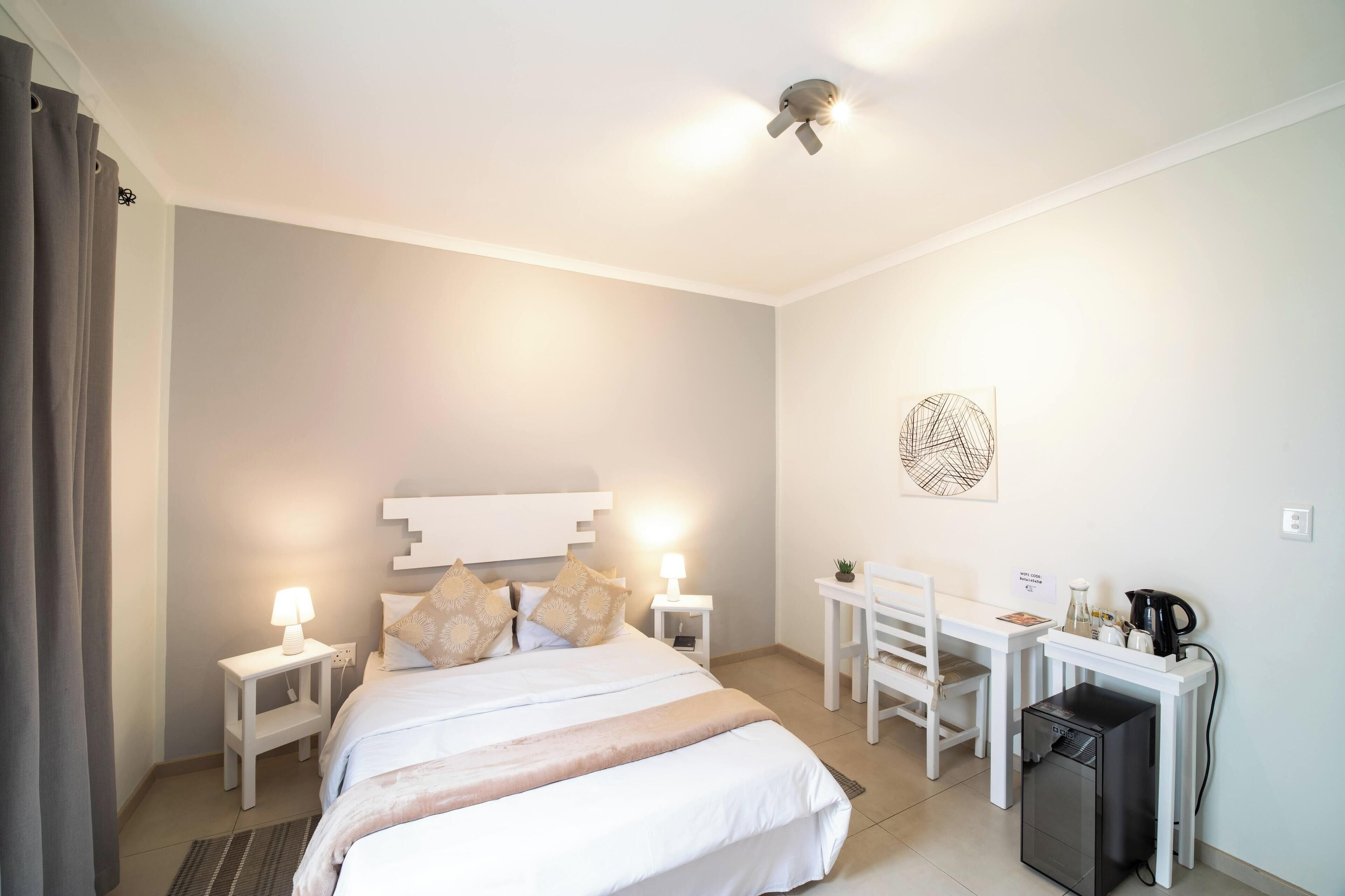 Quarto de hotel com cama, mesas de cabeceira, escrivaninha, cadeira, máquina de café e frigorífico.
