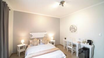 Quarto de hotel com cama, mesas de cabeceira, escrivaninha, cadeira, máquina de café e frigorífico.