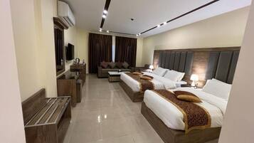 Quarto de hotel com duas camas, um sofá, uma TV e uma mesa com luminária.