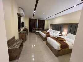 Quarto de hotel com duas camas, um sofá, uma TV e uma mesa com luminária.