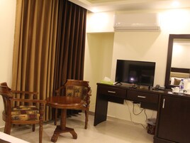 Quarto de hotel com escrivaninha de madeira, televisão, cadeira e uma janela grande com cortinas.