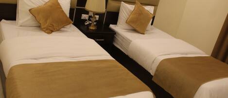 Quarto de hotel com duas camas, cada uma com roupa de cama branca e mantas marrons. Há uma mesa de cabeceira com abajur e telefone entre as camas.
