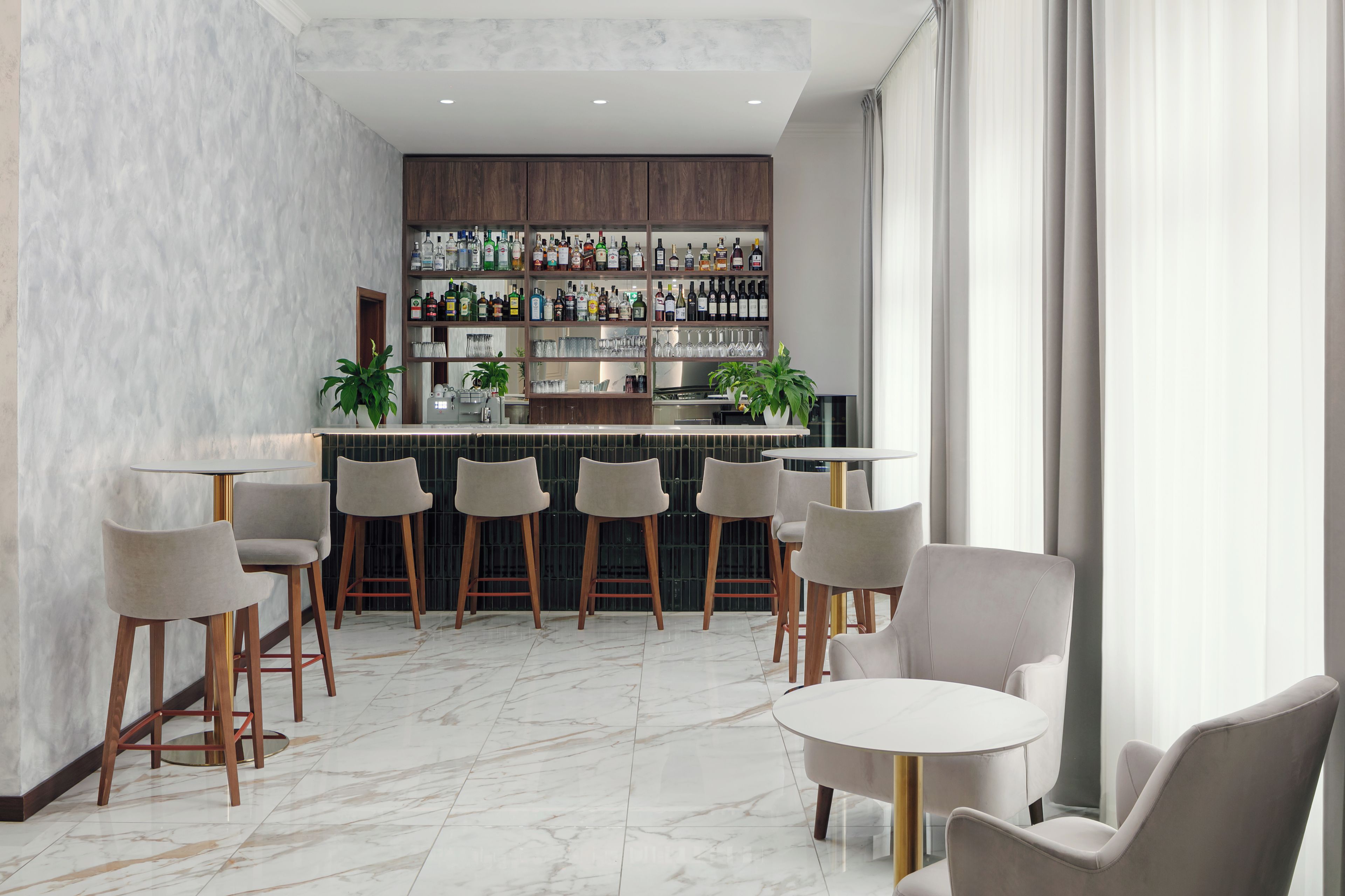 Uma área de bar com piso de mármore, cadeiras de madeira e balcão repleto de garrafas.