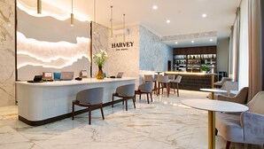 Uma área de recepção moderna com piso de mármore, balcão de recepção, algumas cadeiras, um espaço de bar e uma parede com a placa de um hotel spa.