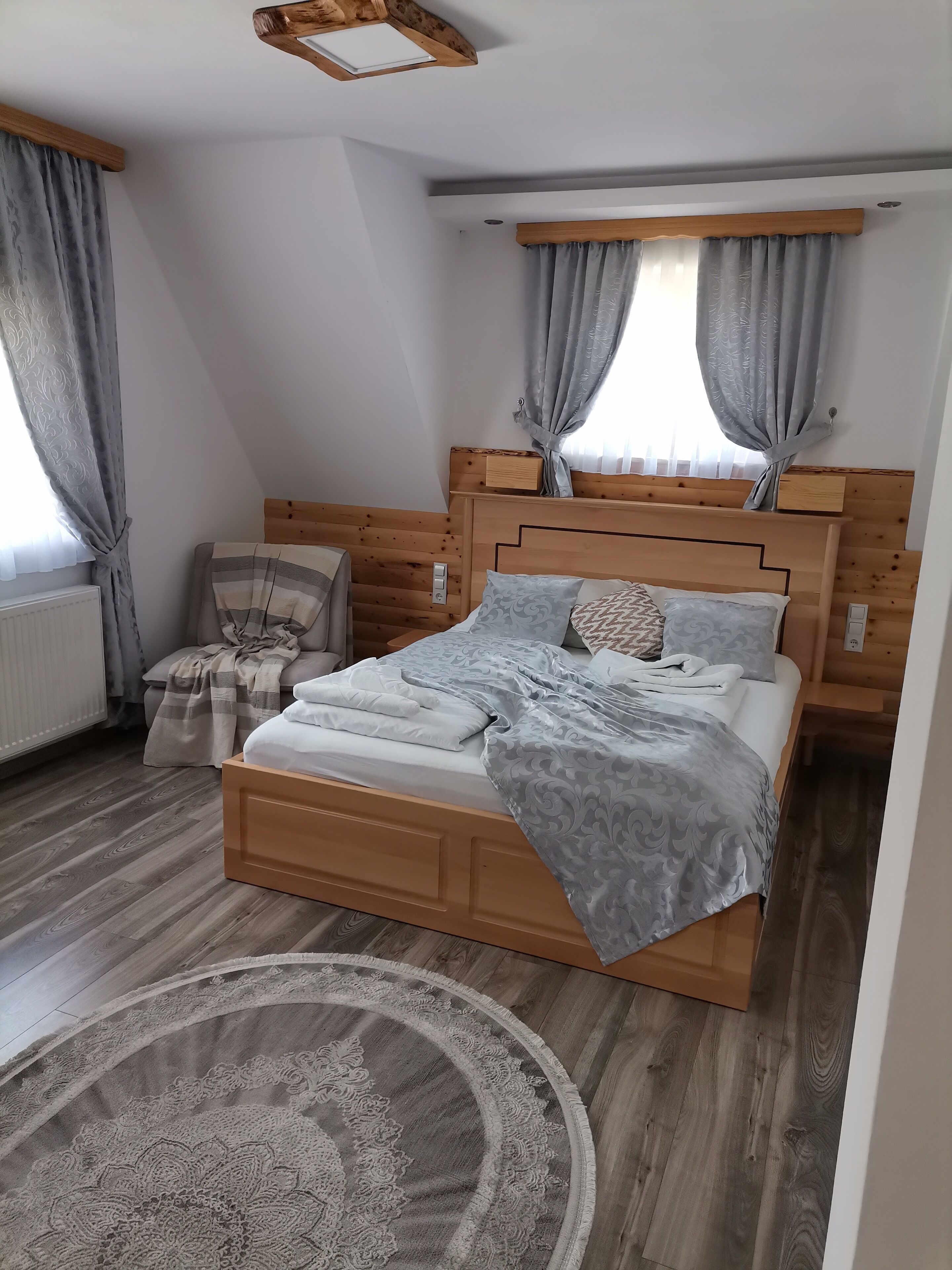 Quarto com cama de madeira, roupa de cama cinza estampada, tapete cinza e branco estampado e cabeceira de madeira.