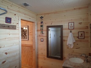 Casa de banho de cabana de madeira com porta de madeira, espelho, lavatório e toalha pendurada na parede.