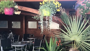 Uma área externa com mesas e cadeiras, cercada por vasos de plantas e arranjos florais pendentes.