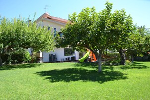 Uma casa com telhado vermelho, um escorrega verde e um gramado bem cuidado.