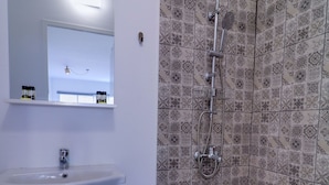 Um banheiro com pia branca, espelho, chuveiro com chuveiro manual e azulejos estampados.