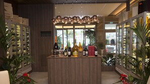 Zona de bar com balcão de madeira, garrafas de vinho e copos. Há plantas em vasos e vista para o exterior através de grandes janelas.