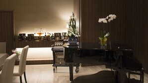 Quarto com piano, área de bar com garrafas e copos, e uma orquídea branca em vaso.