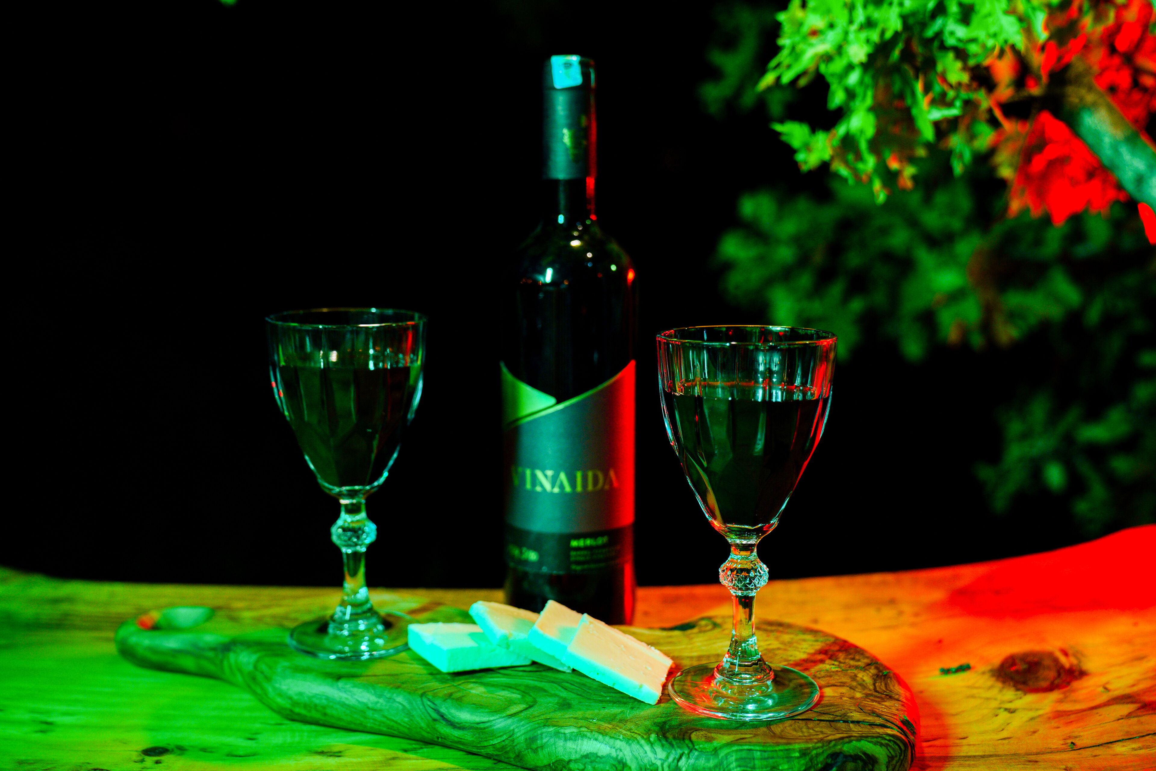 Uma garrafa de vinho e duas taças de vinho sobre uma superfície de madeira, com fundo escuro.
