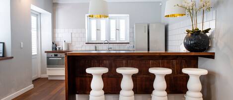 Uma cozinha moderna com uma ilha central, banquetas de madeira, armários brancos e uma janela ampla.