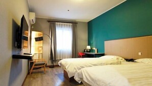 Quarto de hotel com duas camas, uma escrivaninha, uma cadeira, televisão e janela com cortinas.