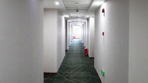 Um corredor comprido e estreito com paredes brancas e chão com padrão verde, que leva a uma extremidade iluminada.