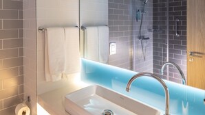 Uma casa de banho moderna com uma sanita branca, um espelho e zona de duche.