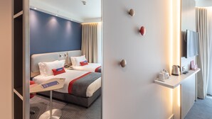 Quarto de hotel com cama, mesa de cabeceira e televisão de tela plana na parede.