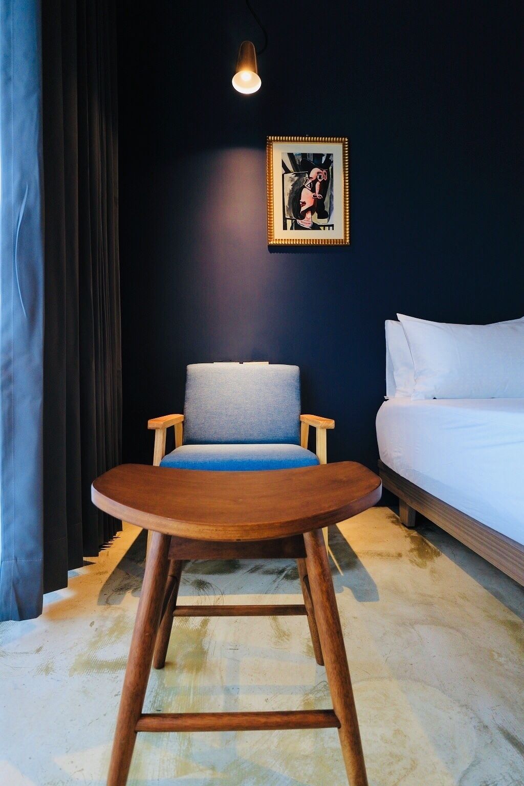 Um quarto com uma mesa de madeira, uma cadeira azul, uma cama e um quadro na parede.