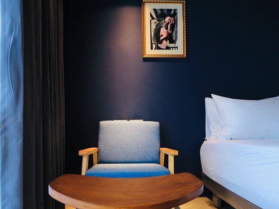 Um quarto com uma mesa de madeira, uma cadeira azul, uma cama e um quadro na parede.
