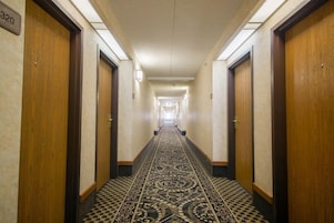 Um corredor de hotel com portas de madeira, carpete estampado e uma placa de número na parede.
