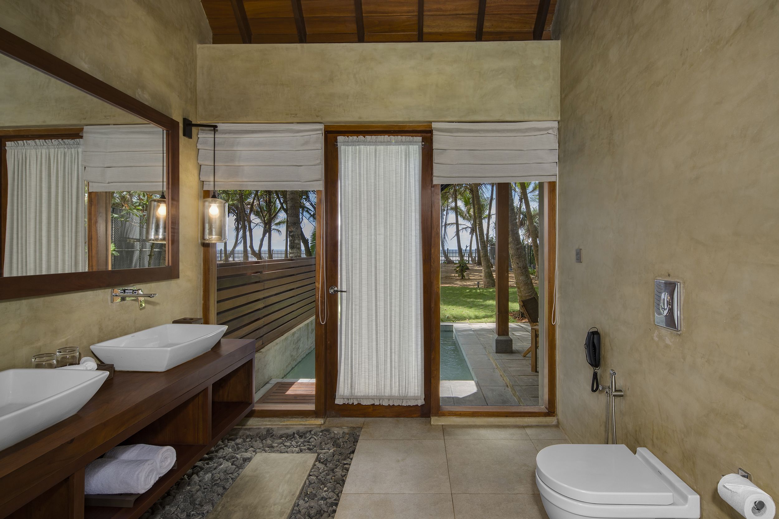 Casa de banho com duas pias, sanita e zona de duche com porta de vidro.