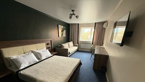 Quarto de hotel com uma cama grande, um sofá, uma escrivaninha e uma janela com cortinas.