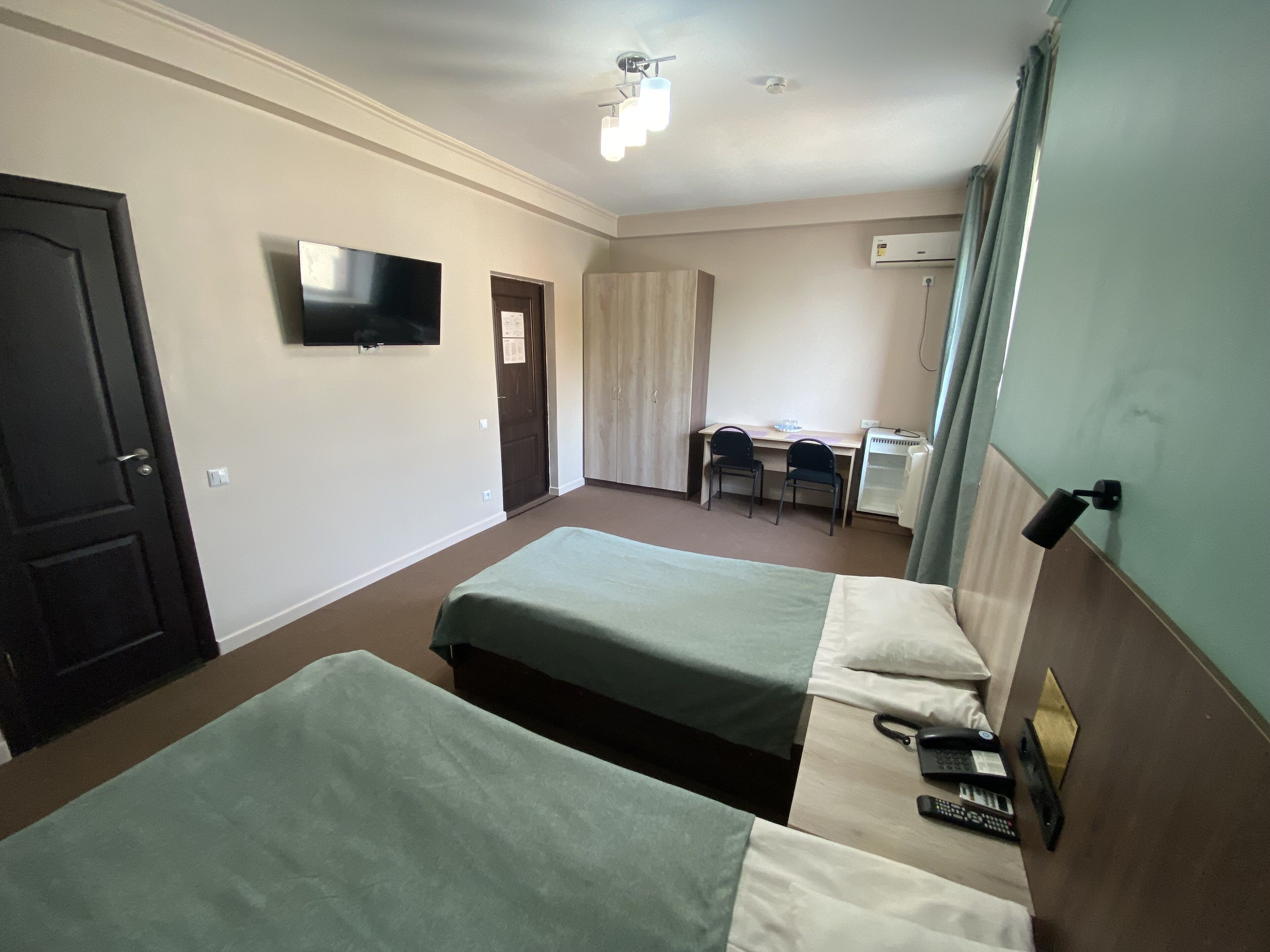 Quarto de hotel com duas camas, uma secretária com duas cadeiras, uma televisão e um ar condicionado.