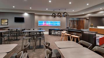 Um hall de hotel moderno com várias áreas de estar, um balcão de recepção e um grande painel digital.