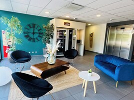 Um lobby moderno com parede verde-água, um relógio grande, uma mesa de recepção e um sofá azul.