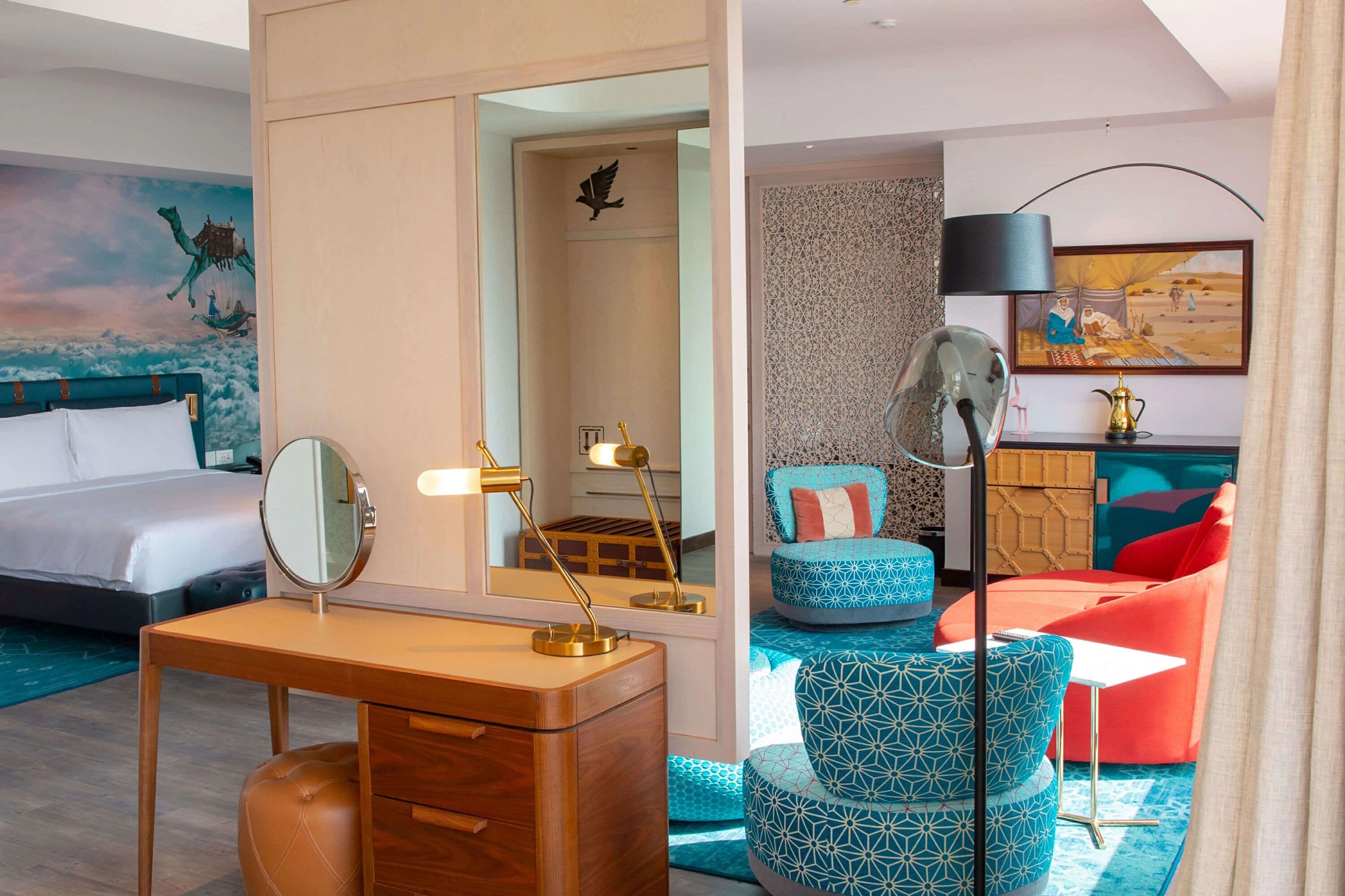 Quarto de hotel com uma cama, uma toucador com espelho, uma escrivaninha, uma cadeira e um sofá.