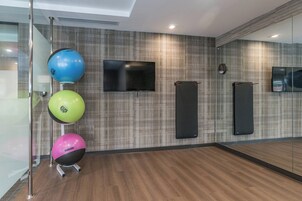 Uma sala de ginástica com bolas de exercício, uma televisão e equipamentos de exercício fixados na parede.