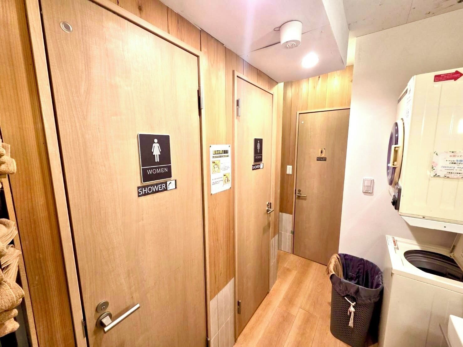Um corredor com portas de madeira, algumas identificadas para mulheres e chuveiros, e uma área de lavanderia com uma máquina de lavar.