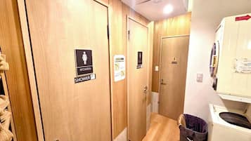 Um corredor com portas de madeira, algumas identificadas para mulheres e chuveiros, e uma área de lavanderia com uma máquina de lavar.