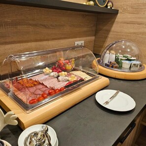 Disposição de buffet com diversos alimentos sob uma cúpula de vidro, um prato com garfo e uma pequena tigela com acompanhamentos.