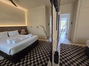 Quarto de hotel com uma cama grande, roupa de cama branca, chão xadrez e vista para o corredor.
