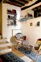 Quarto com escada, radiador, estante de livros, espelho e cadeira com almofada colorida.