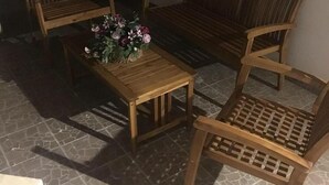 Um banco de madeira, uma mesa de madeira com um arranjo floral e uma cadeira de madeira sobre um piso de azulejos.