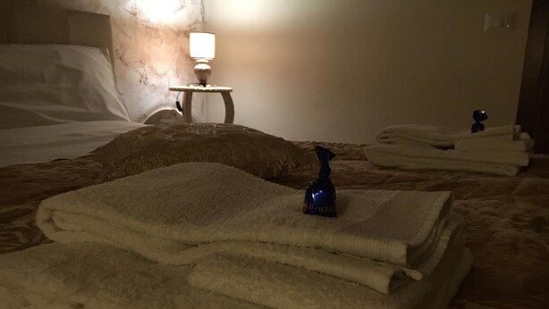 Cama bem arrumada com toalhas dobradas e um frasco de álcool em gel.