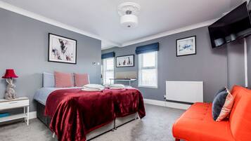 Quarto com cama, sofá vermelho, mesa de cabeceira branca e luminária vermelha.