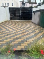Uma área pavimentada com padrão xadrez, um portão preto e uma porta verde.