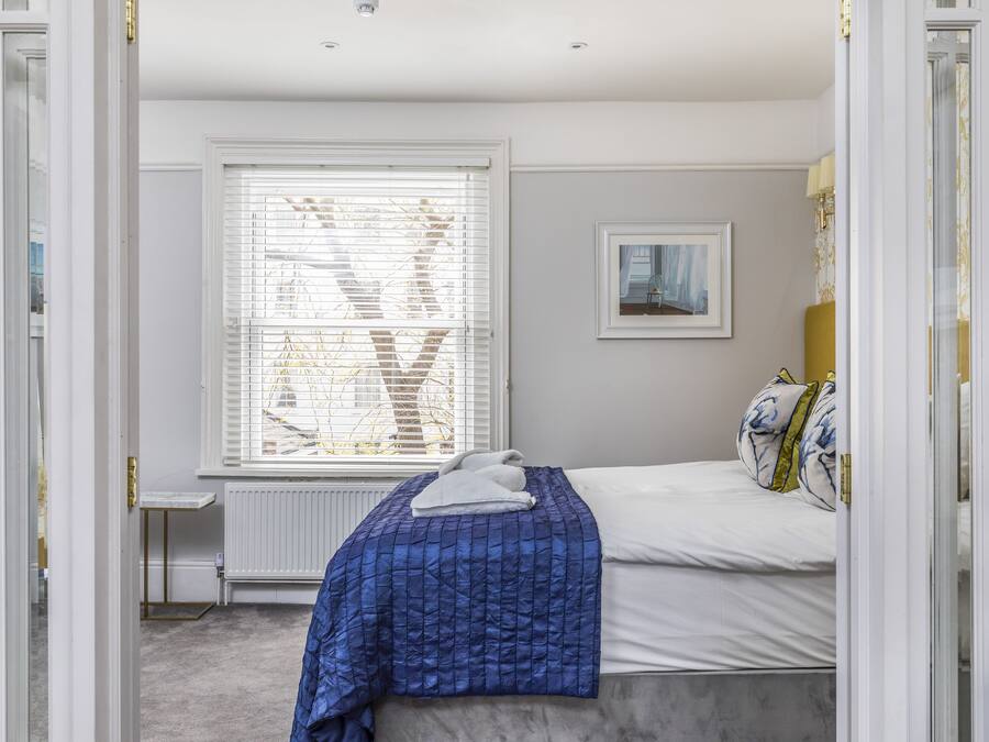 Quarto com cama, radiador, janela com persianas, mesa de cabeceira e um quadro na parede.