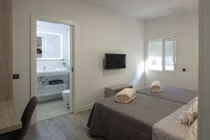 Quarto de hotel com cama, televisão, banheiro com pia e vaso sanitário, e janela com persianas.