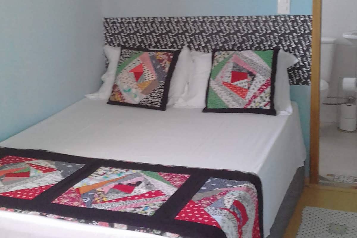 Uma cama com um edredom estampado, uma cabeceira com um design preto e branco e uma pequena mesa de cabeceira com uma luminária branca.