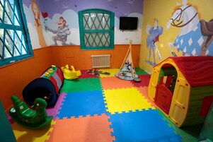 Uma sala de jogos com tapetes de espuma coloridos, uma casinha e um mural na parede.