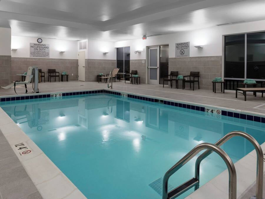 Piscina interior com cadeira de salva-vidas, espreguiçadeiras e aviso de proibição de mergulho.