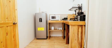 Cozinha compacta com geladeira, micro-ondas e bancada de madeira.