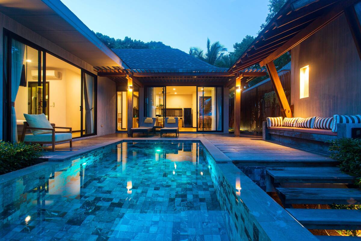 Uma área de piscina ao ar livre moderna, com piso de azulejos, rodeada por um deck de madeira e espreguiçadeiras.