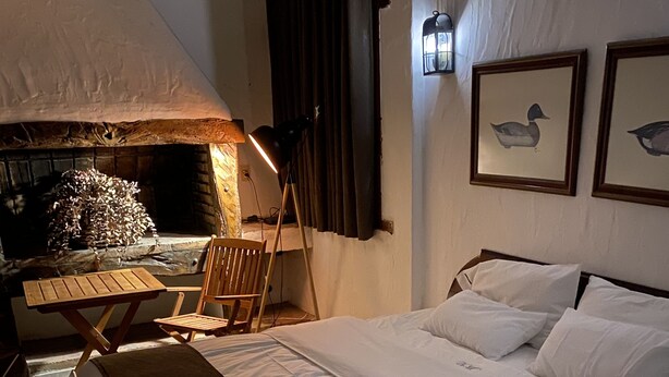 Quarto de hotel com cama, uma cadeira de madeira, uma mesa pequena e lareira.
