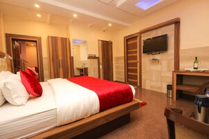 Quarto de hotel moderno com uma cama grande, guarda-roupa de madeira, televisão na parede e uma pequena escrivaninha com uma garrafa e um copo.