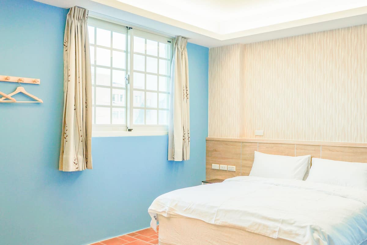 Quarto com cama, janela com cortinas, cabeceira de madeira e prateleira fixada na parede.